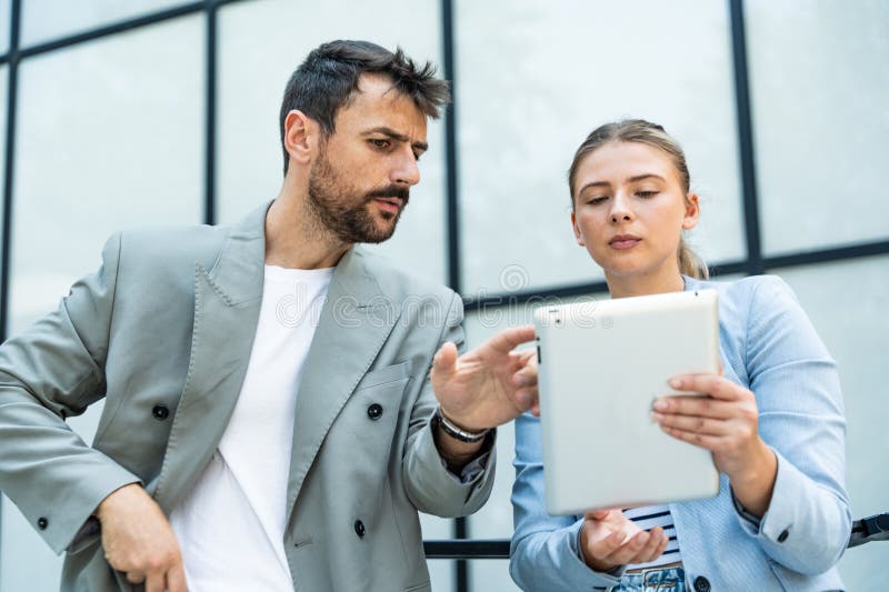 Two Coworkers Using a Digital Tablet and Talking while Standing Outside ...