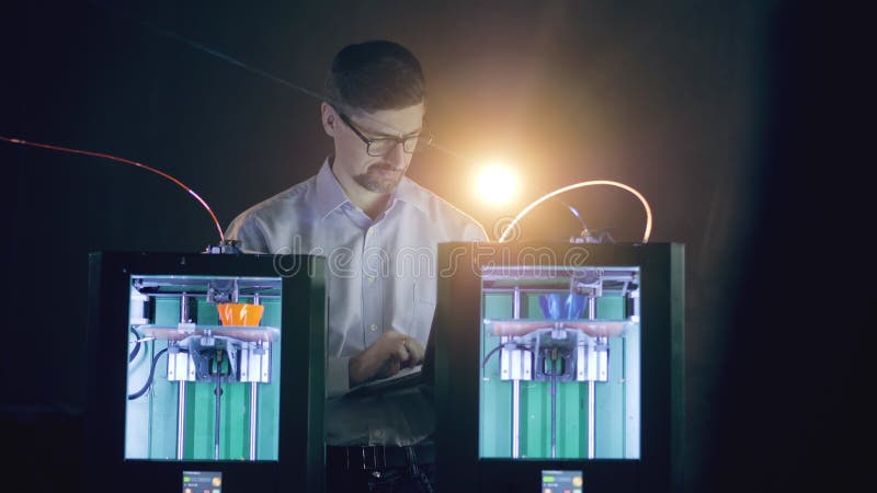 Two 3D-printers are Working in a Dark Room with a Male Engineer Stock ...