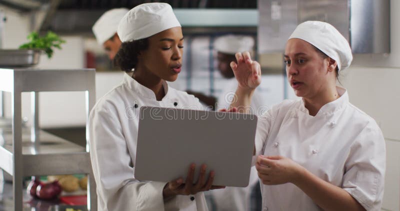 Two Diverse Female Chefs Talking and Using Laptop in Restaurant Kitchen ...