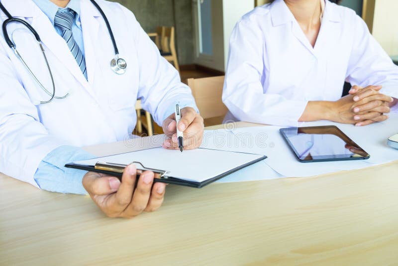 Two Doctors Discussing Patient Notes in an Office Pointing To a Stock ...