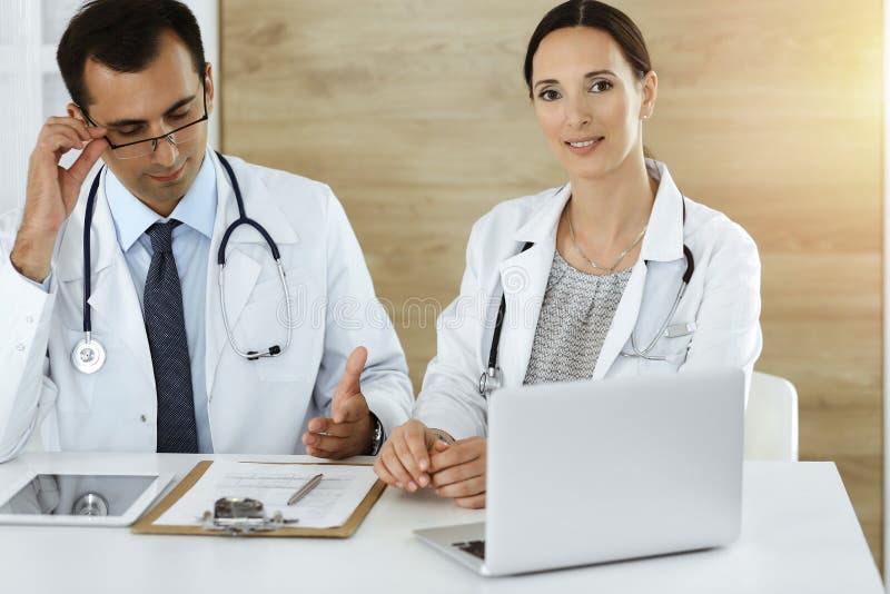Two Doctors Discussing Treatment Problems while Sitting at the Desk in ...