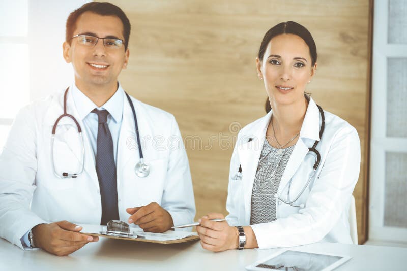 Two Doctors Discussing Treatment Problems while Sitting at the Desk in ...