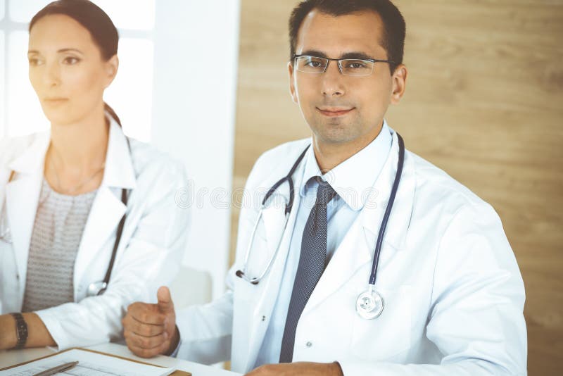 Two Doctors Discussing Treatment Problems while Sitting at the Desk in ...