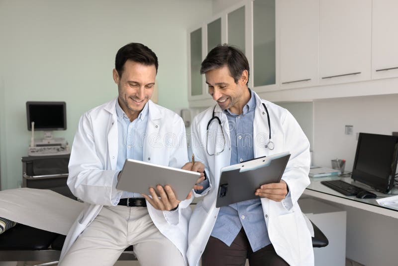 Two Doctors Smiling while Reviewing Information on Tablet and Clipboard ...