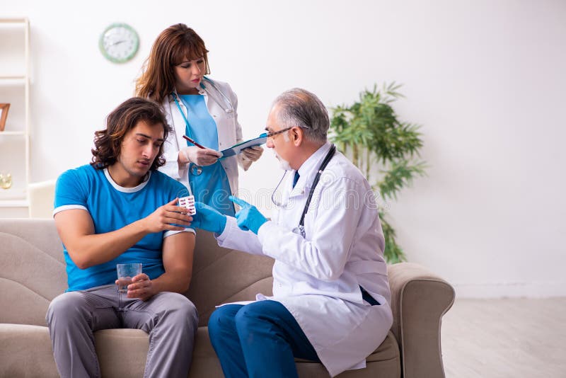 Two Doctors Visiting Sick Young Man at Home Stock Photo - Image of ...
