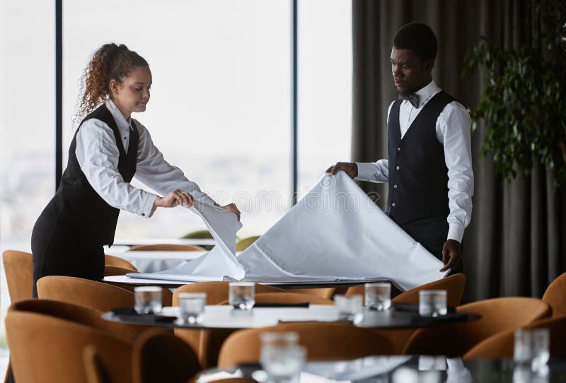 Two Elegant Servers Setting Tables with White Tablecloths in Restaurant ...