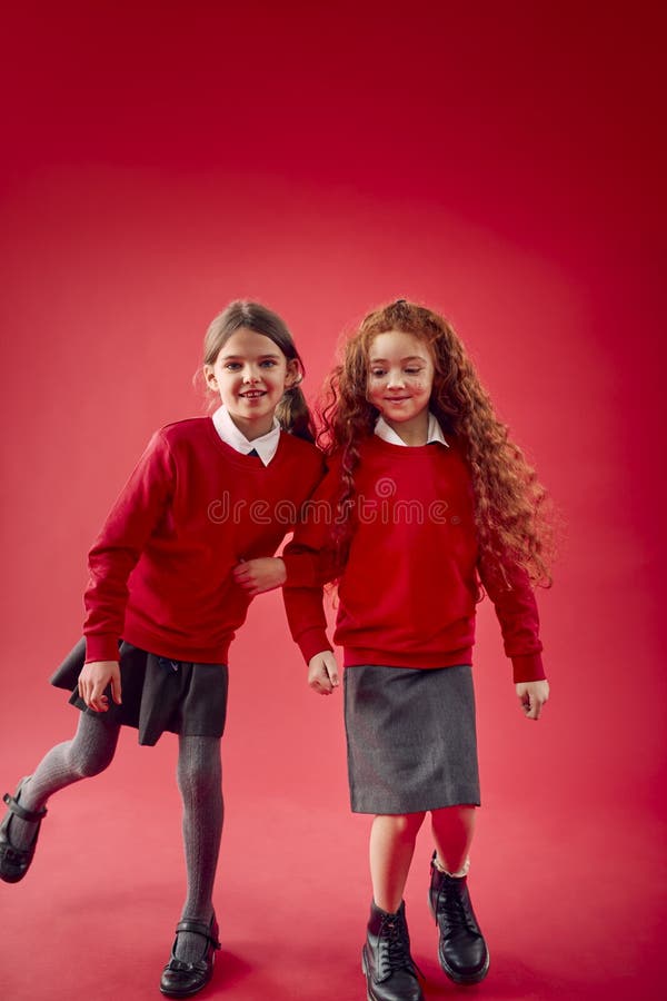 Two Elementary School Pupils Wearing Uniform Linking Arms Against Red ...