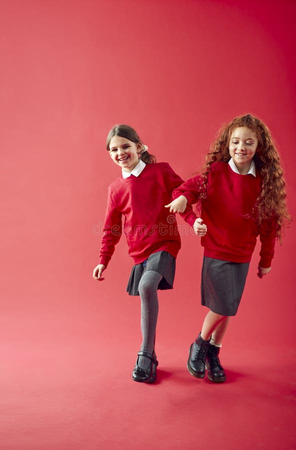 Two Elementary School Pupils Wearing Uniform Linking Arms Against Red ...