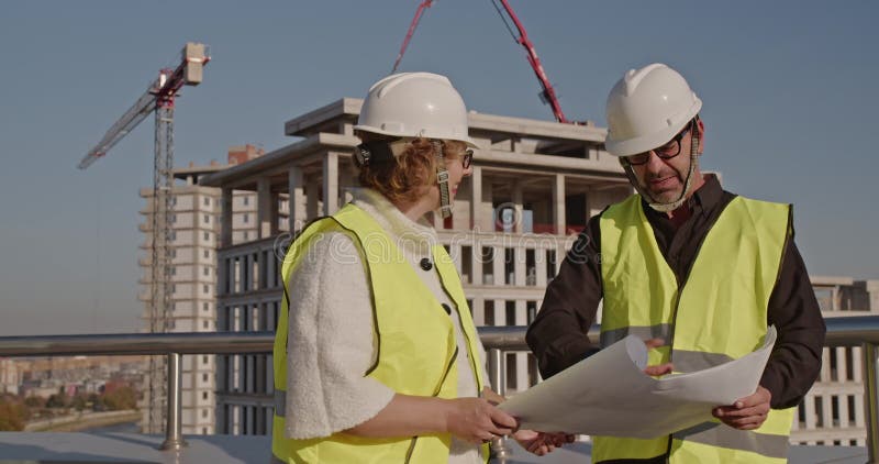 Engineers Discussing Blueprints at Construction Site with Unfinished ...