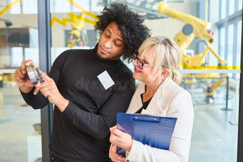 Engineers Discussing Robotics Component in Industrial Setting with Gripper Arms in Background ...