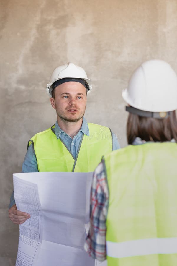 Two Engineers, a Man and a Woman in White Helmets and Protective Vests ...