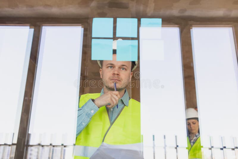 Two Engineers in Protective Vests and White Helmets Glue Stickers on ...