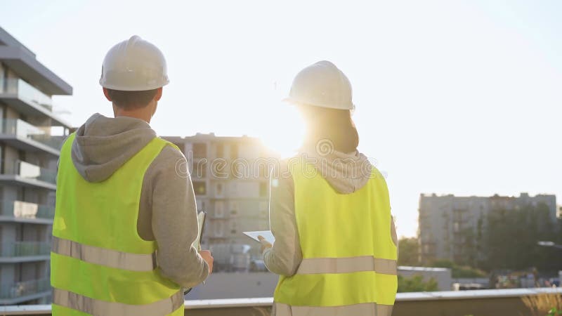 Two Engineers are Standing on a Construction Site Wearing Hard Hats and ...