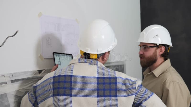 Two Engineers are Standing at the Wall with Drawings and Discussing the ...