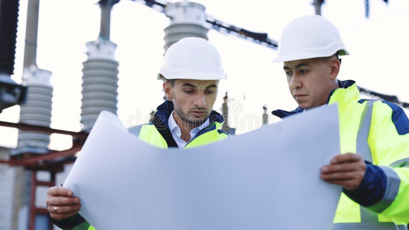 Two Engineers are Talking in Front of Electrical Transmission Lines ...