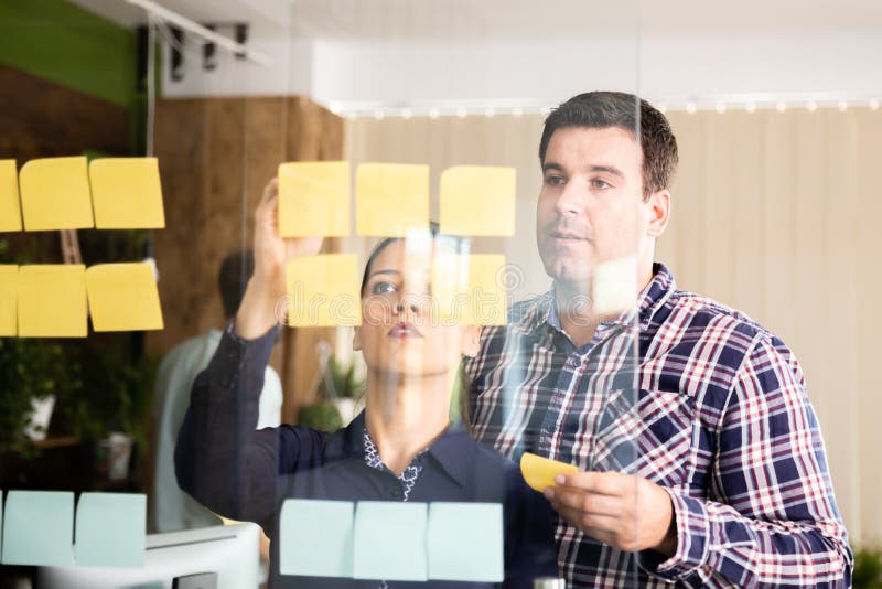 Two Entrepreneurs Looking at Sticky Notes on a Glass Window Stock Image ...