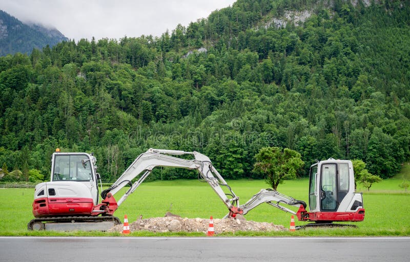 Two Excavators Working Together on Roadside Construction in Green ...