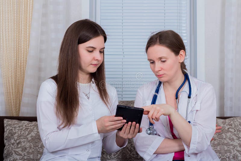 Two Female Doctors or Nurses Look at the Tablet and Discuss Therapy ...