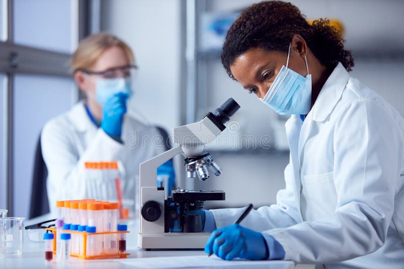 Two Female Lab Workers Wearing PPE and Safety Glasses Looking at Slide ...