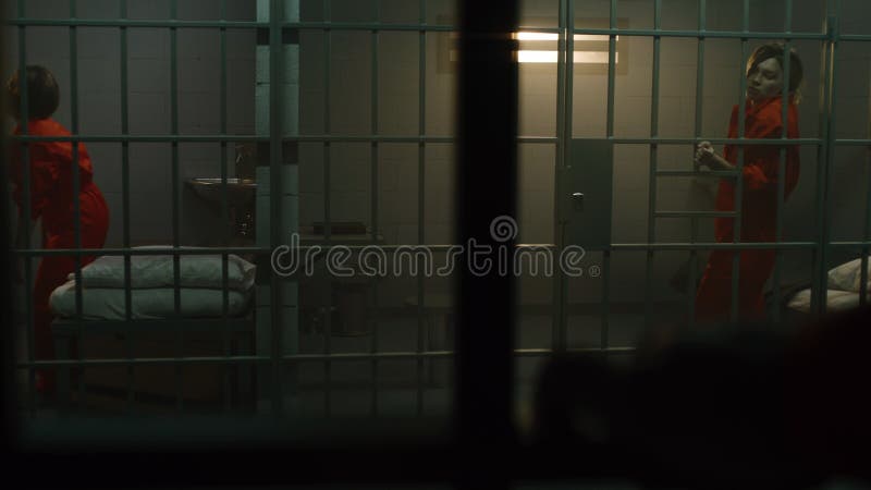 Two Female Prisoners Stand Facing the Metal Bars in Front of Prison ...
