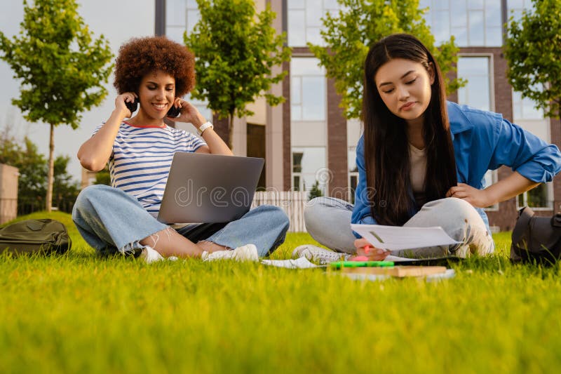 Two Female Students Doing Homework Together while Sitting on Lawn in ...