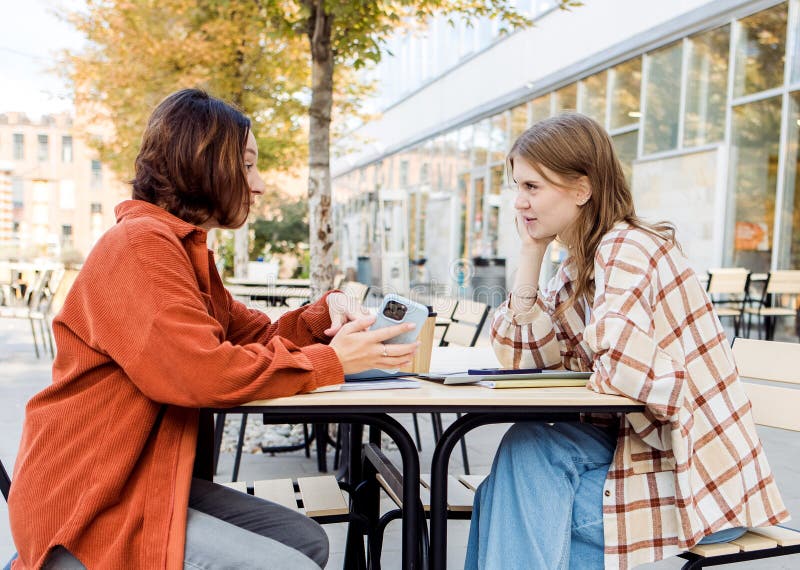 Two Female Students are Sitting at a Table Outside and Discussing Their ...