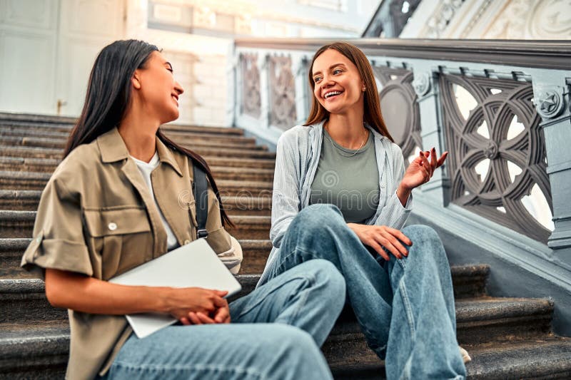Two Female Students are Talking while Sitting on the Steps of the ...