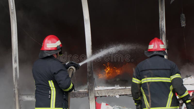 Two Firefighters in Safety Uniform and Helmets Extinguishing the Fire ...