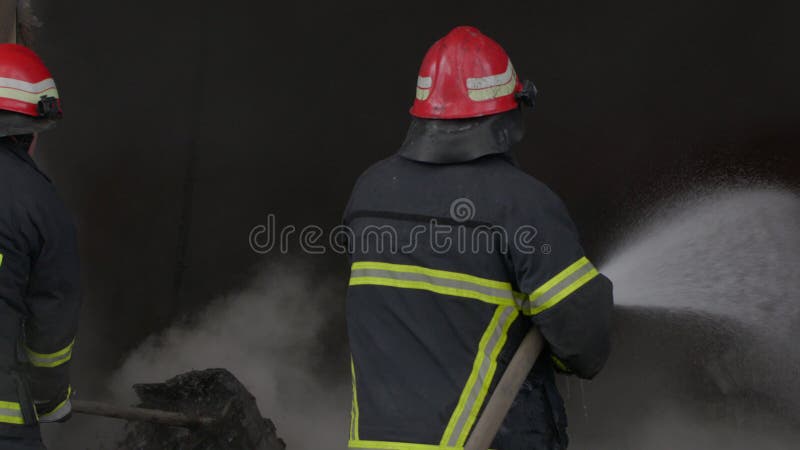 Two Firefighters in Safety Uniform and Helmets Extinguishing a Fire ...