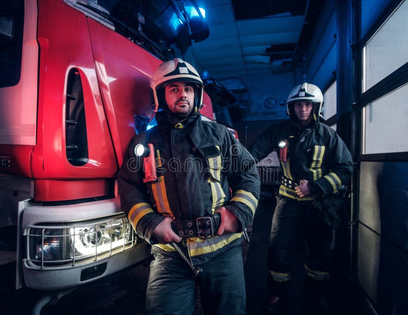 Two Firemen Wearing Protective Uniform Standing Next To a Fire Truck in ...