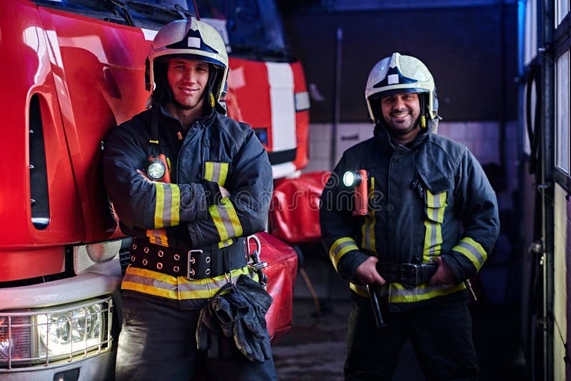 Two Firemen Wearing Uniform Standing Next To a Fire Engine in a Garage ...