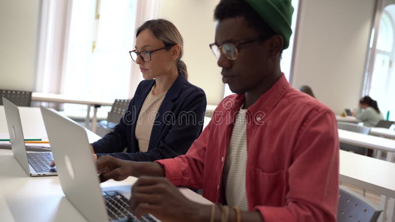 Two Focused Multiracial Students Man and Woman Using Laptops while ...