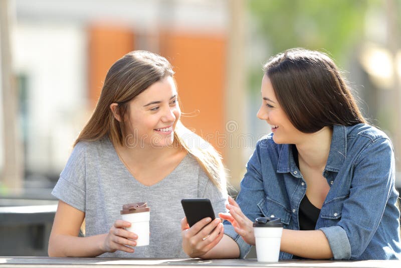 Two Friends Talking about Phone Content in a Park Stock Image - Image ...