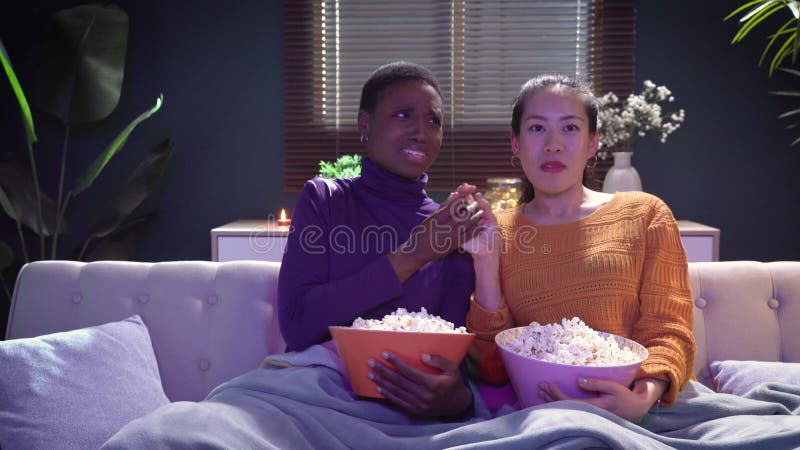 Two Girl Friends Sitting On Couch Watch A Scary Movie And Eat Popcorn Friends Relaxing Together