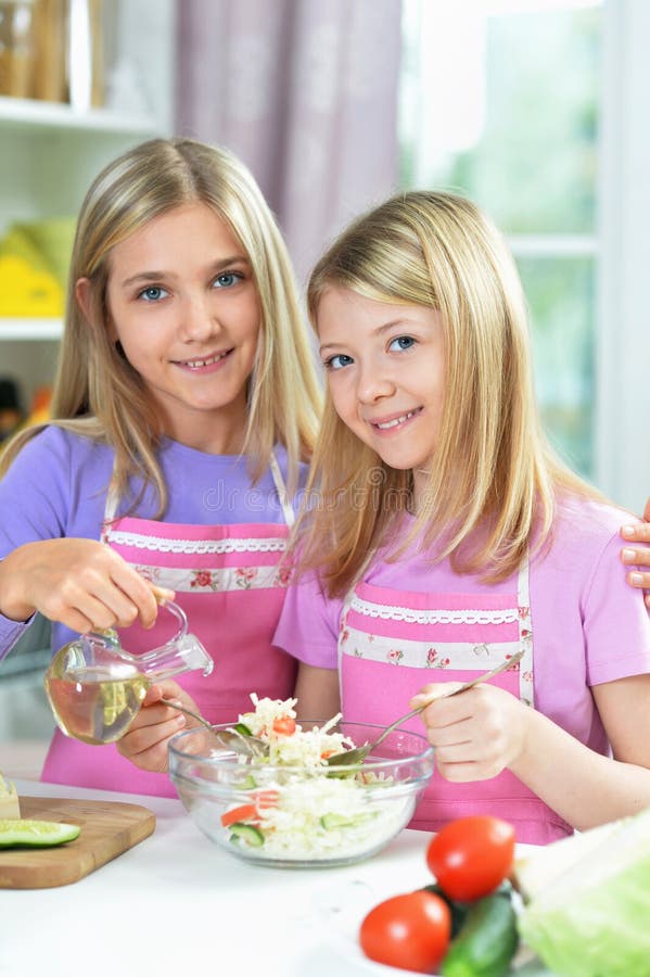 Two Girls in Pink Aprons Preparing Salad on Kitchen Table Stock Photo ...