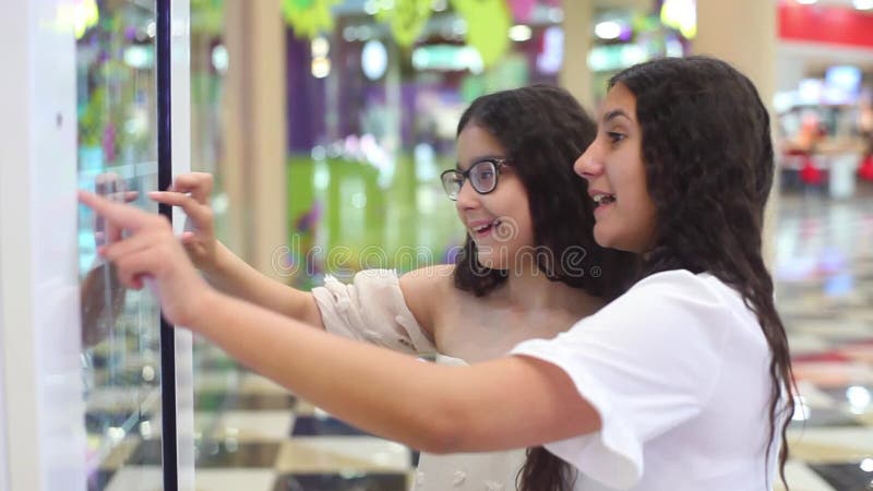 Two Girls Use the Interactive Panel in the Mall. Girls Choose the Goods ...