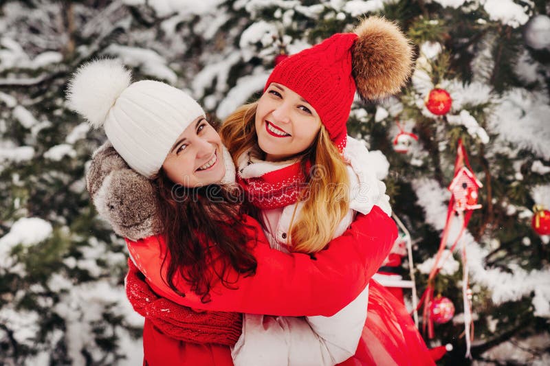 Two Girls In The Winter Forest Hug Warmly Near The Christmas Tree Stock