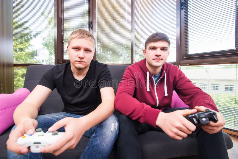 Two Handsome Young Men Playing Video Games while Sitting on Sofa Stock ...