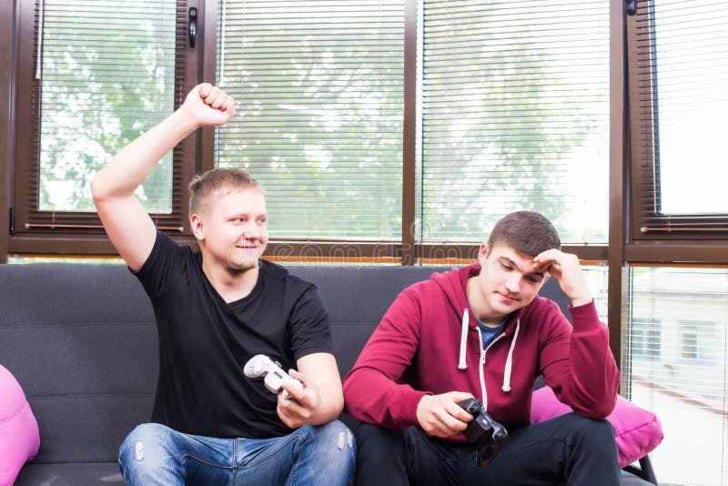 Two Handsome Young Men Playing Video Games while Sitting on Sofa Stock ...