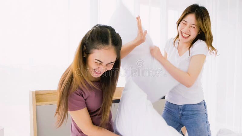 Two Happy And Attractive Asian Women Having A Pillow Fight With Smiles