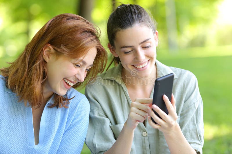 Two Happy Friends Laughing Checking Phone in a Park Stock Image - Image ...