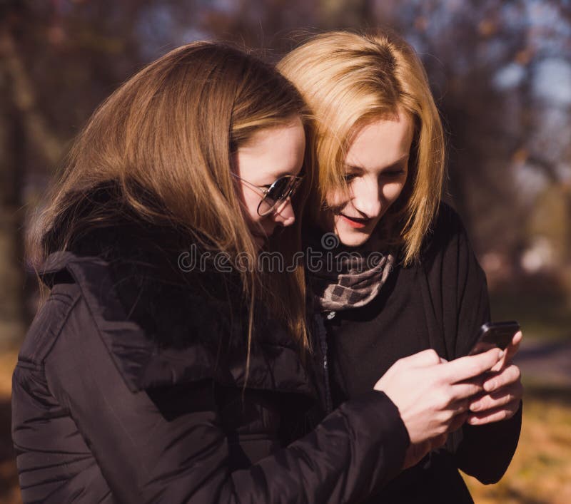 Two Happy Women Friends Sharing Social Media In A Smart Phone Outdoors
