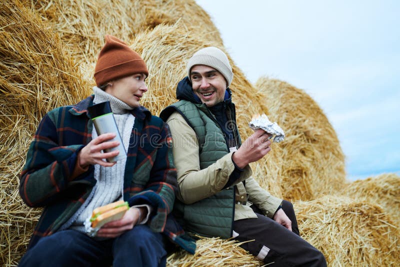 Two Happy Young Workers of Farm Sitting by Stack of Hay and Having ...