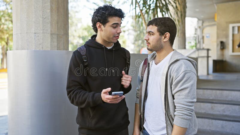 Two Hispanic Men Chatting and Using a Phone on an Outdoor Urban Street ...