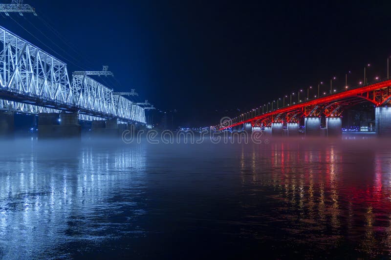 Two Illuminated Bridges at Night Over River with Mist and Reflections ...