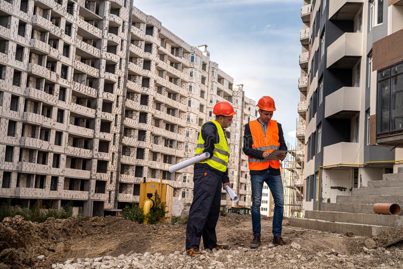 Two Important Workers in Overalls and Helmets Look at the Tablet in the ...