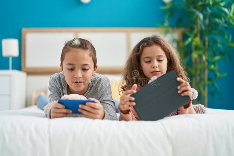 Two Kids Using Smartphone and Touchpad Lying on Bed at Bedroom Stock ...