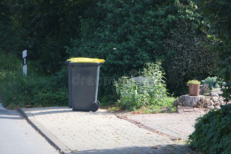 Two Large, Dark Plastic Garbage Cans with Yellow Lids Sit on the Side ...