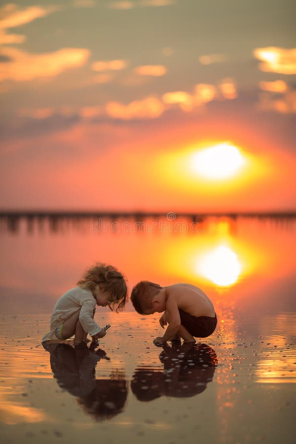 Two Little Children Playing on the Beach during Sunset. Reflection in ...