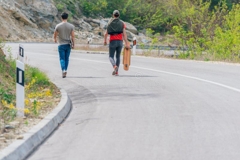 Two Longboarders Holding Their Longboards and Walking Downhill while ...